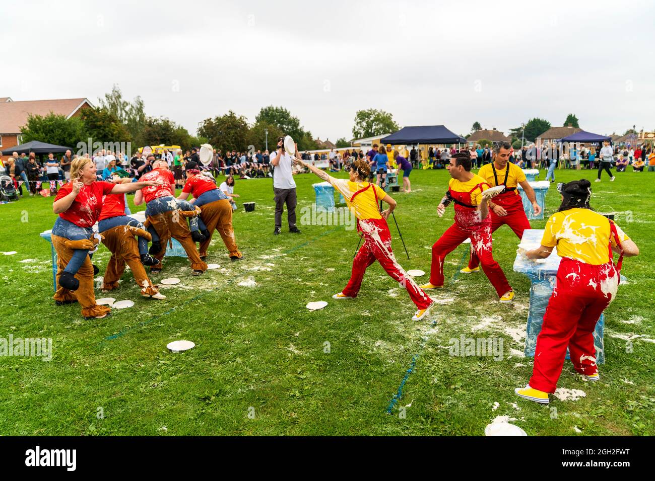 Two teams of four each in fancy dress, in a field, throwing custard ...
