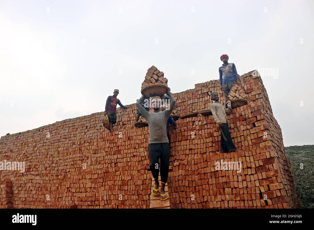 A man holds bricks on her head after taking them out of the ovens ...