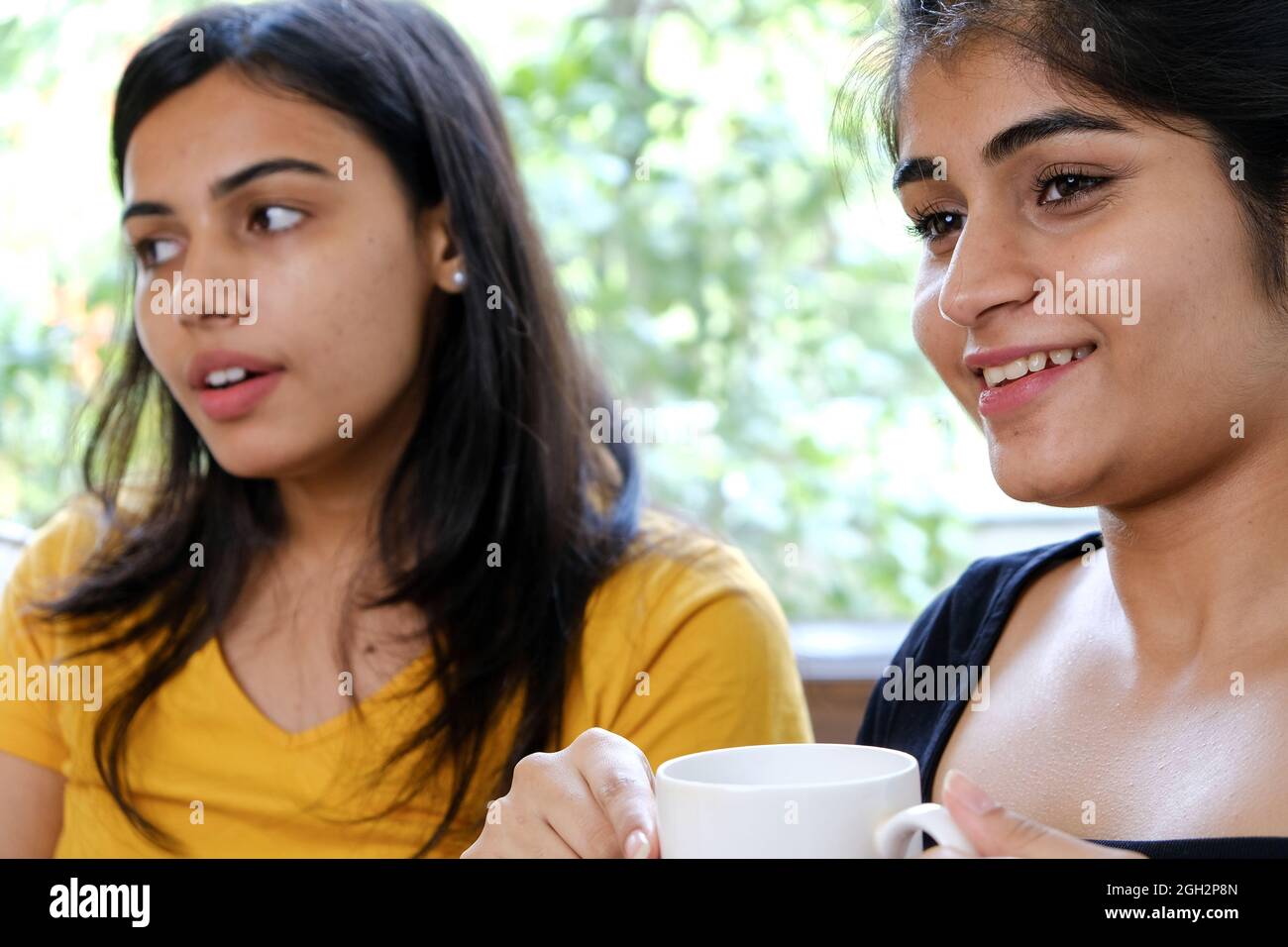 Young Indian girls having a discussion and drinking coffee at home ...