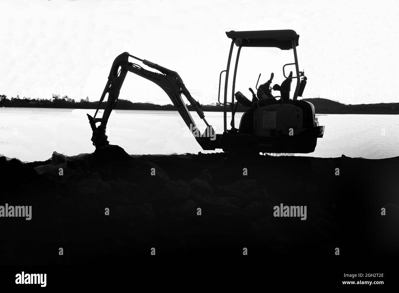 Earth digger standing idle in silhouette on waters edge with land on ...