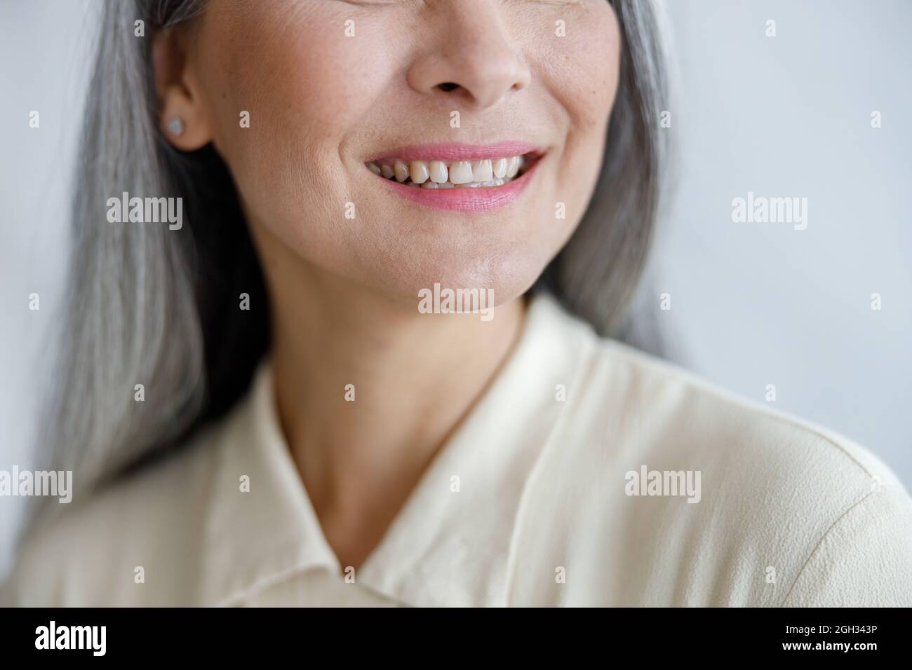Positive mature lady smiles showing healthy teath on light background ...