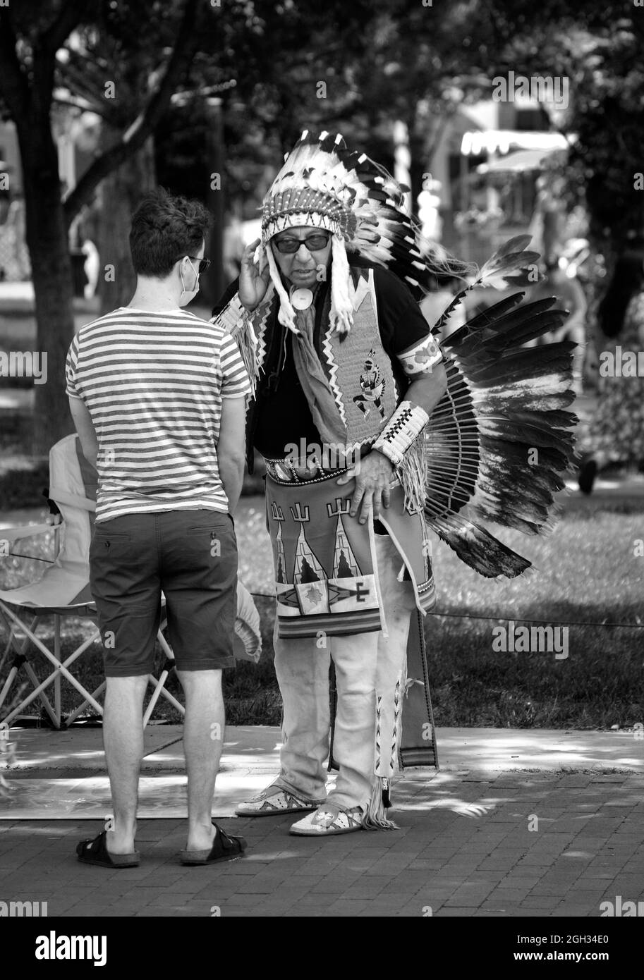 A Native American man dressed in full Plains Indians regalia talks with ...