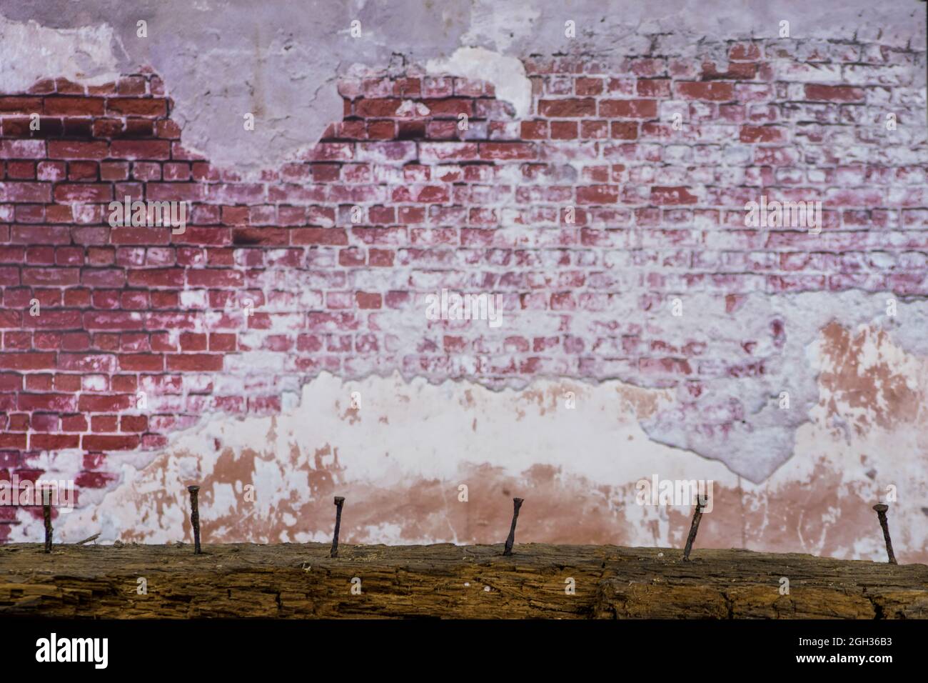 Six rusty nails stuck in a rotten wood beam in front of an old brick ...