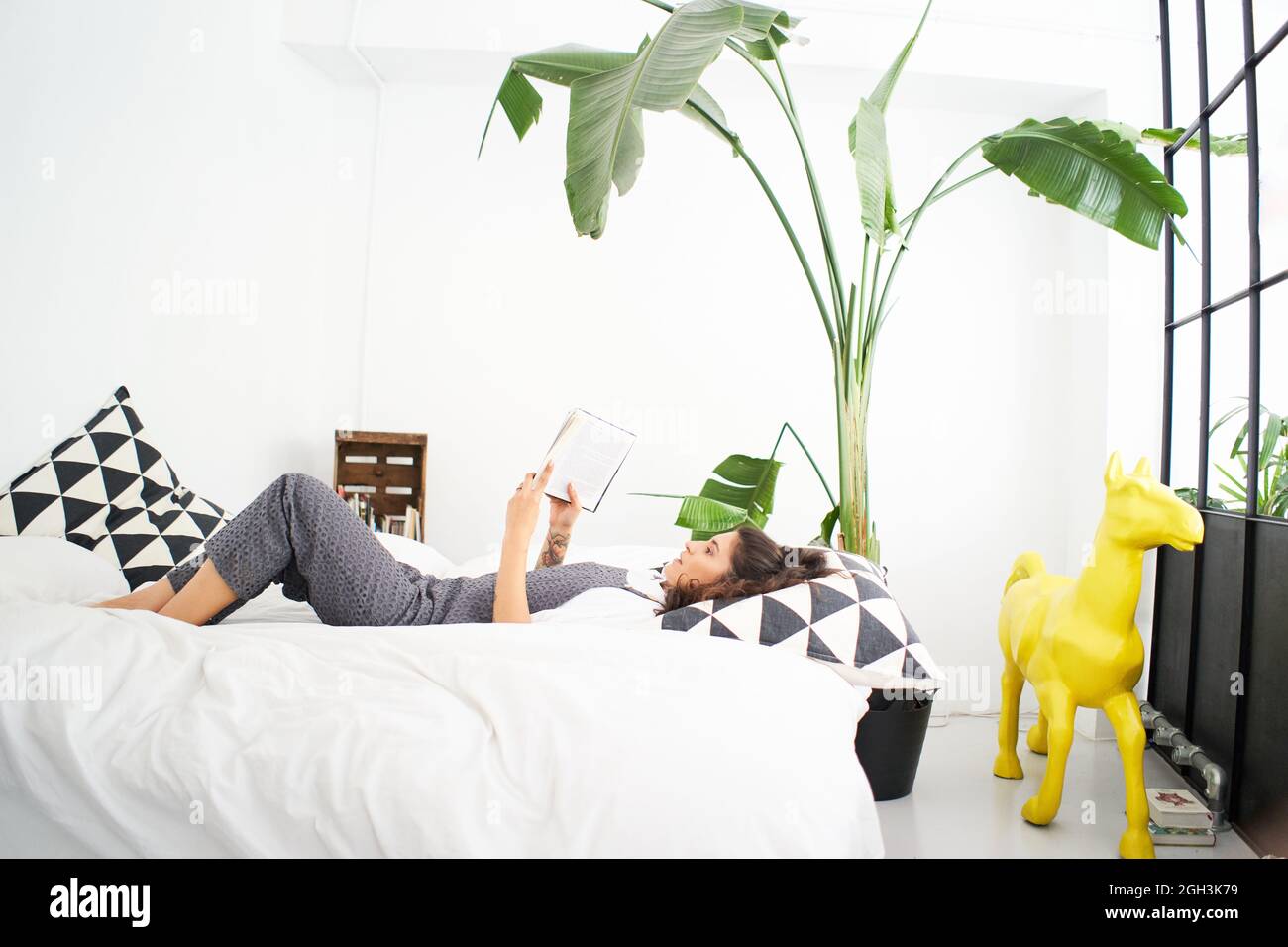 Young latina reads a book in the bedroom lying on the bed enjoying a new day, feeling rested and ...