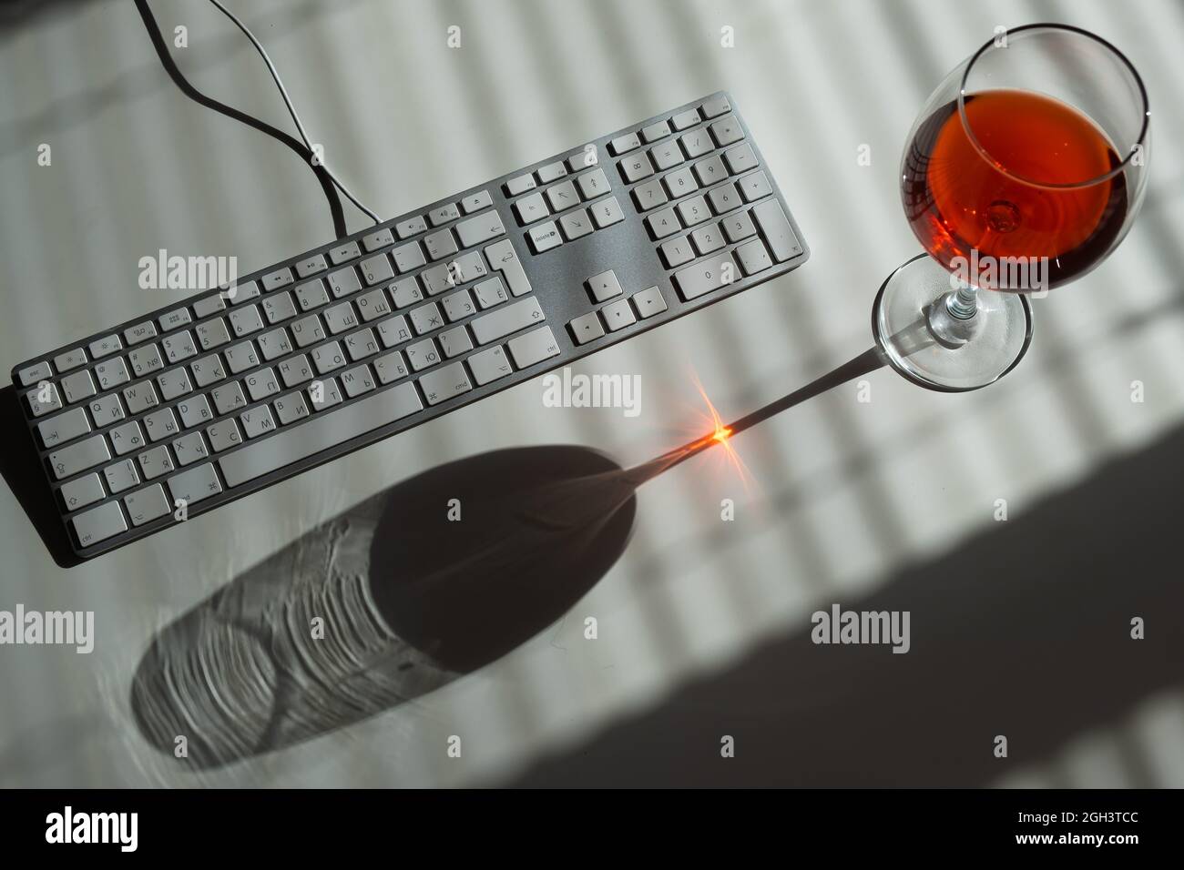 A goblet with red wine and a keyboard on a white table with shade from ...