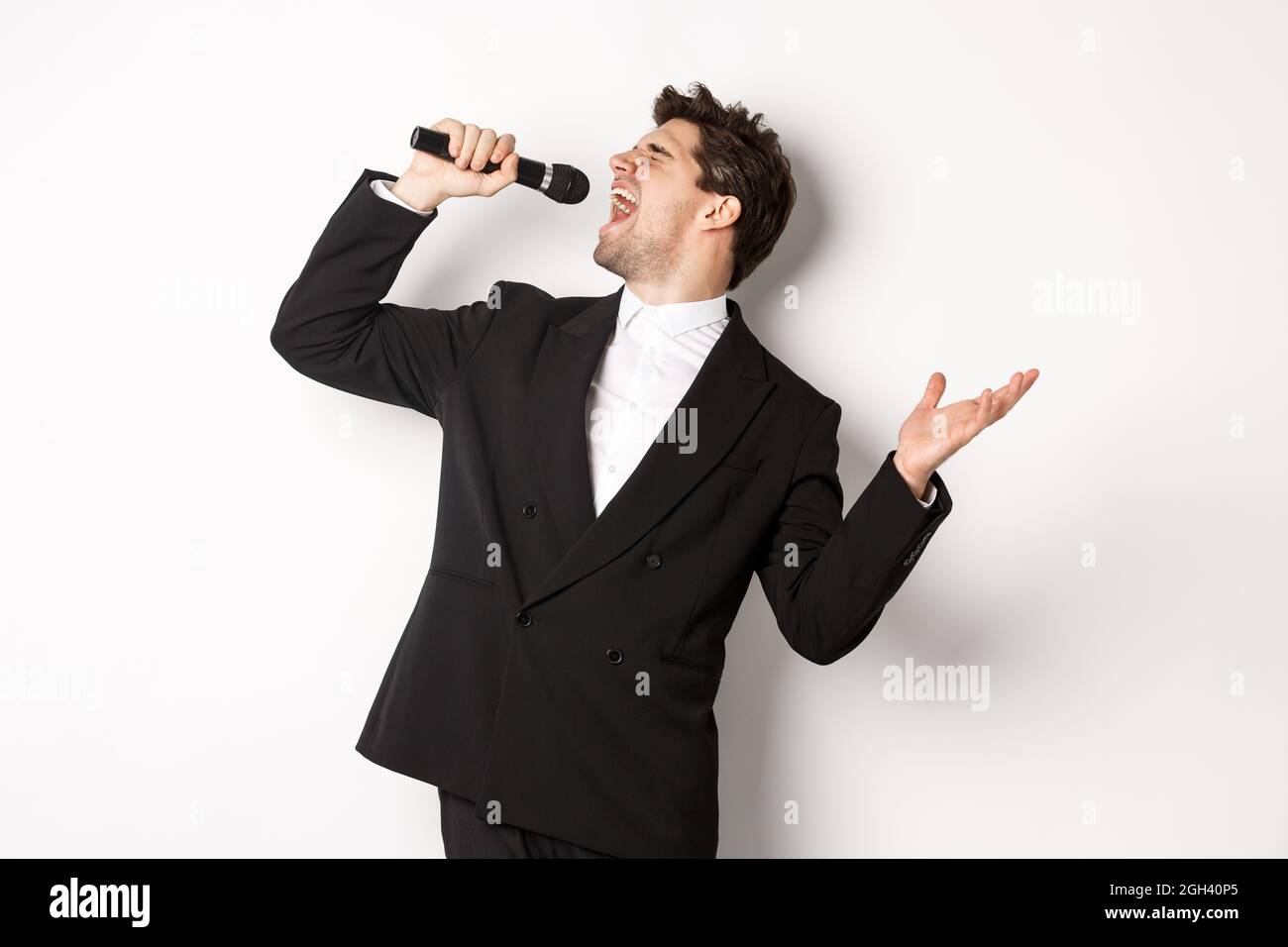 Portrait of handsome man singing a song with passion, standing in black ...