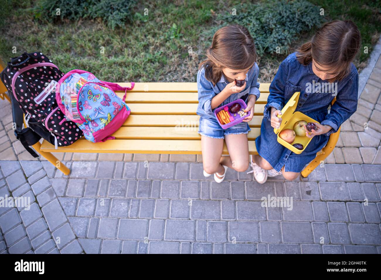 Elementary students sit on a bench near the school and eat fruit for ...