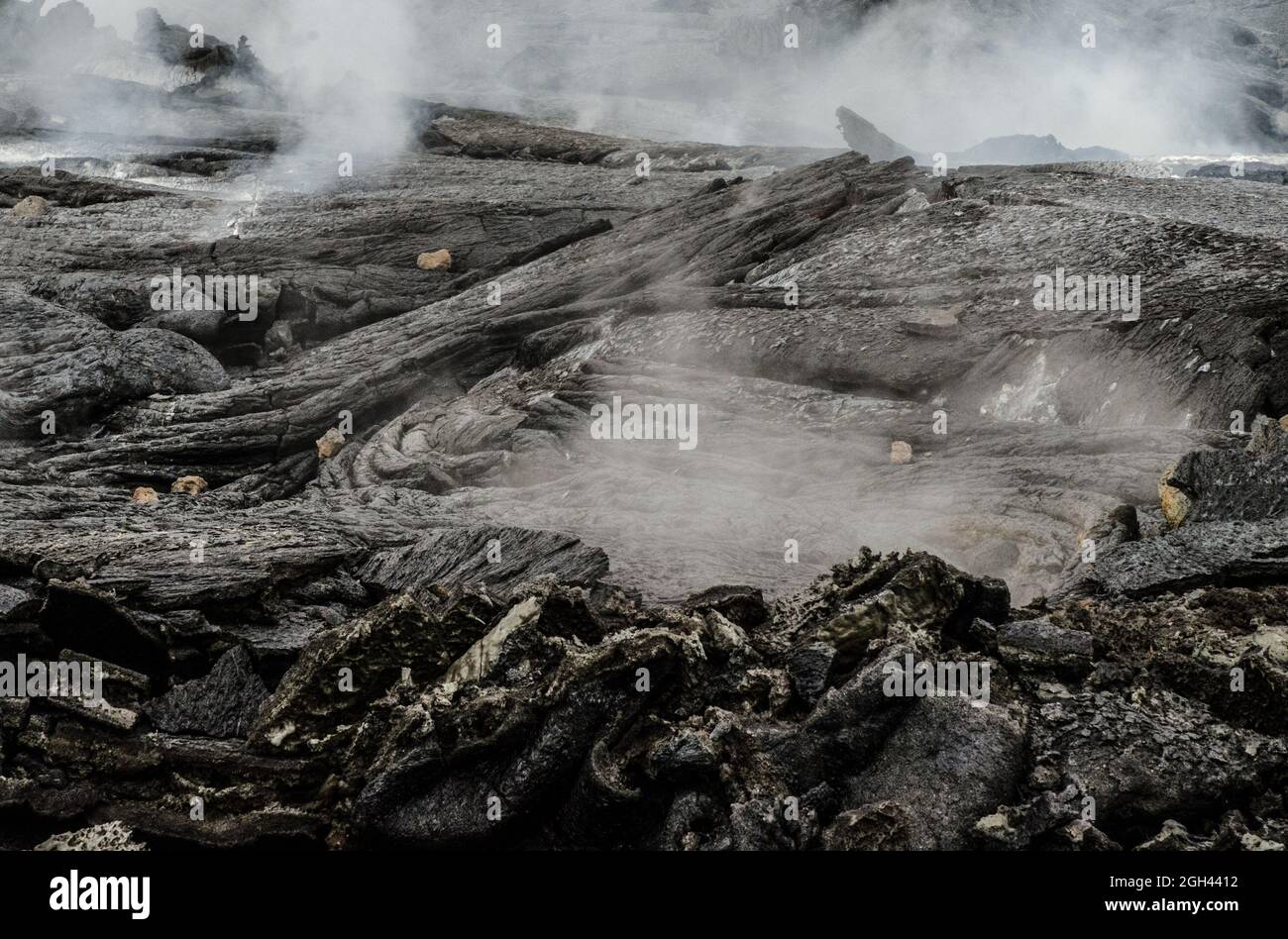 A high angle shot of a landscape with rough volcanic ash and smoke ...