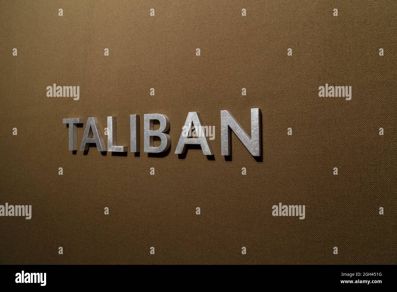 the word taliban laid with silver metal letters on rough tan khaki ...