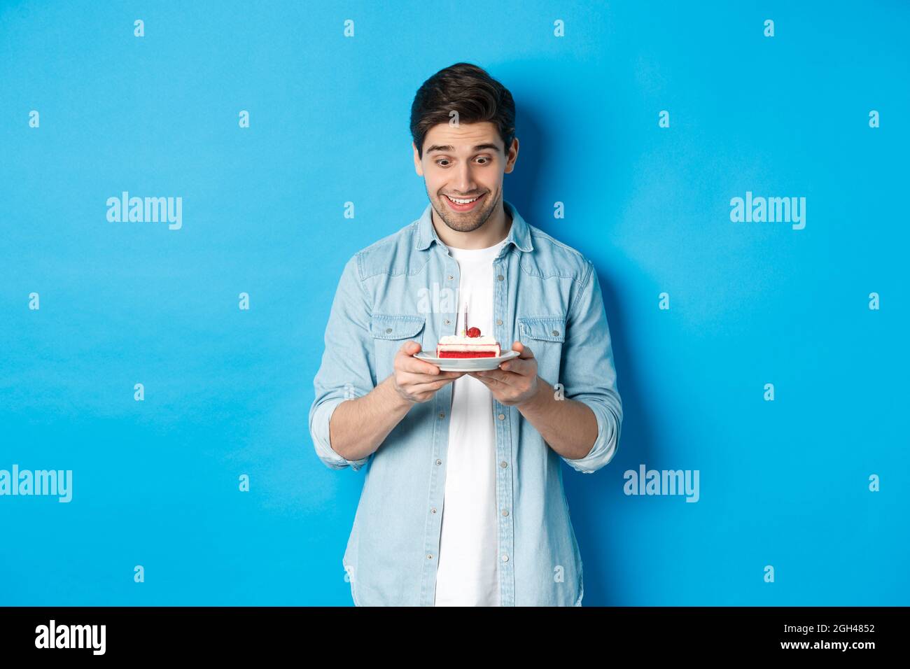 Happy man looking at birthday cake and making with, standing over blue ...