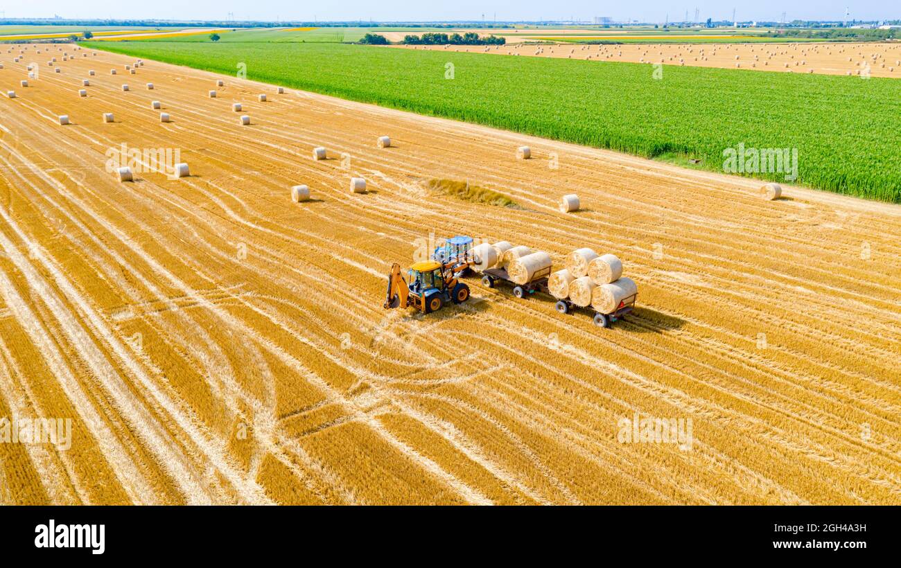 Above view on excavator as loading straw bales on trailer, tow by ...