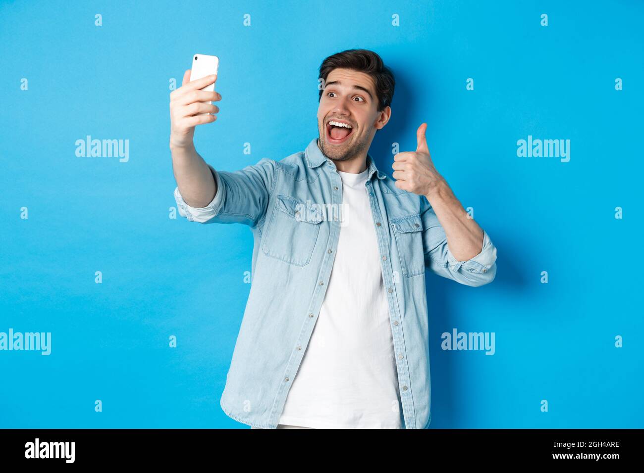 Happy man taking selfie and showing thumb up in approval on blue ...