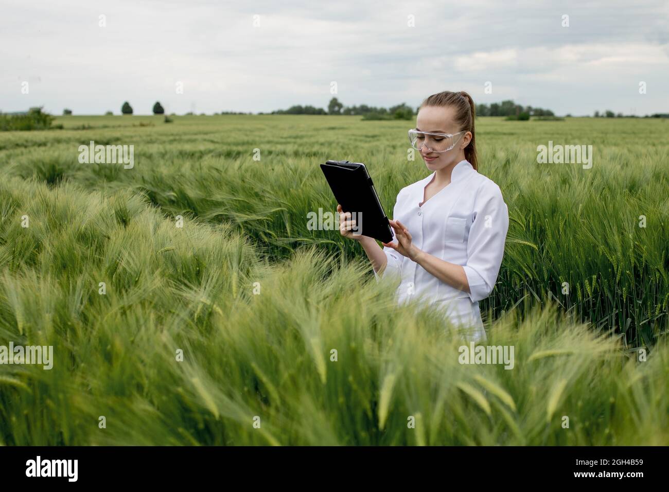Young female ecologist scientist in goggles standing in green field and working on glass ...