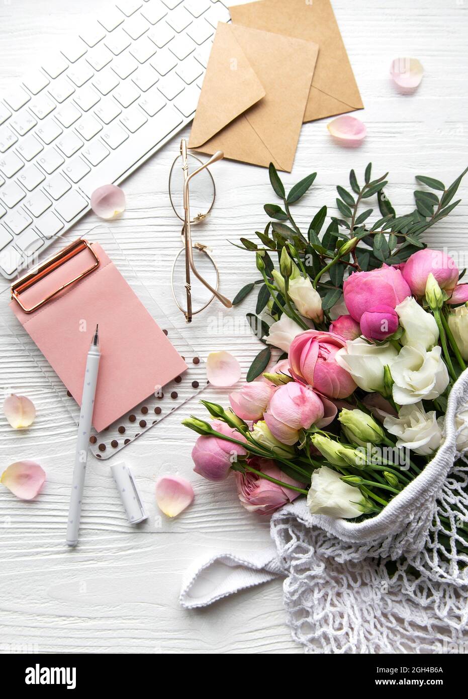 Feminine workspace with keyboard, rose flowers, office supply on a ...