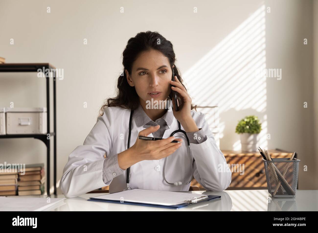 Serious female doctor giving telephone consultation, talking to patient ...