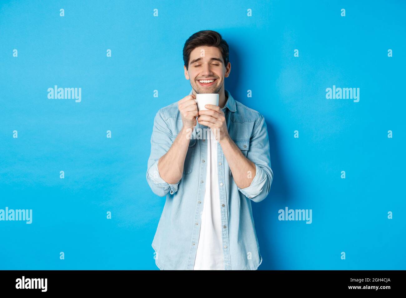 Satisfied man enjoying cup of tea or coffee, holding mug with pleased ...