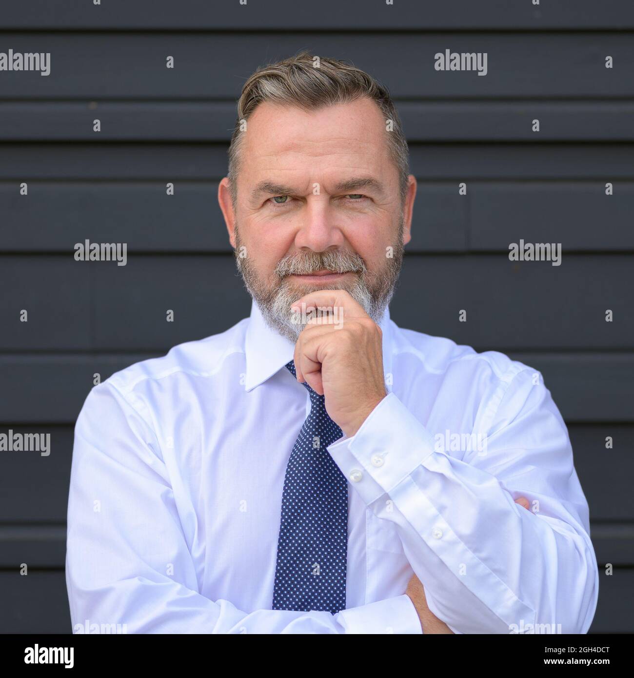 Astute thoughtful businessman staring at the camera with his hand to ...