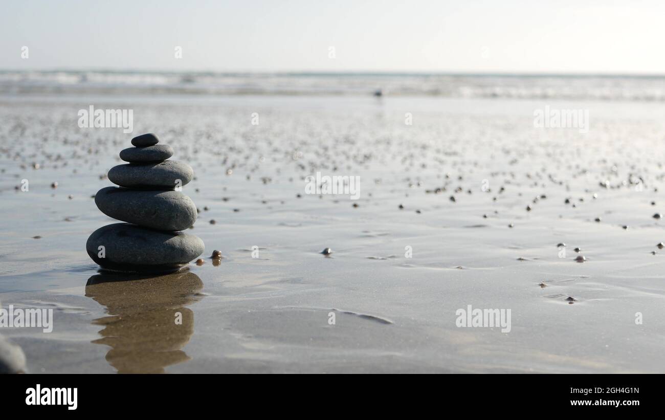 Rock balancing on ocean beach, stones stacking by sea water waves ...