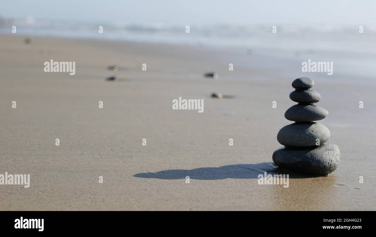 Rock balancing on ocean beach, stones stacking by sea water waves ...
