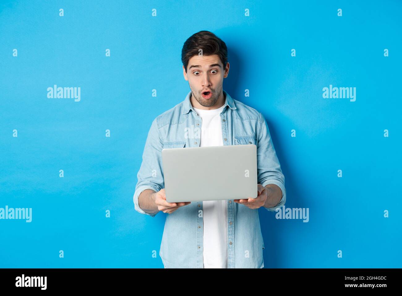 Impressed caucasian guy looking at laptop screen with amazement ...