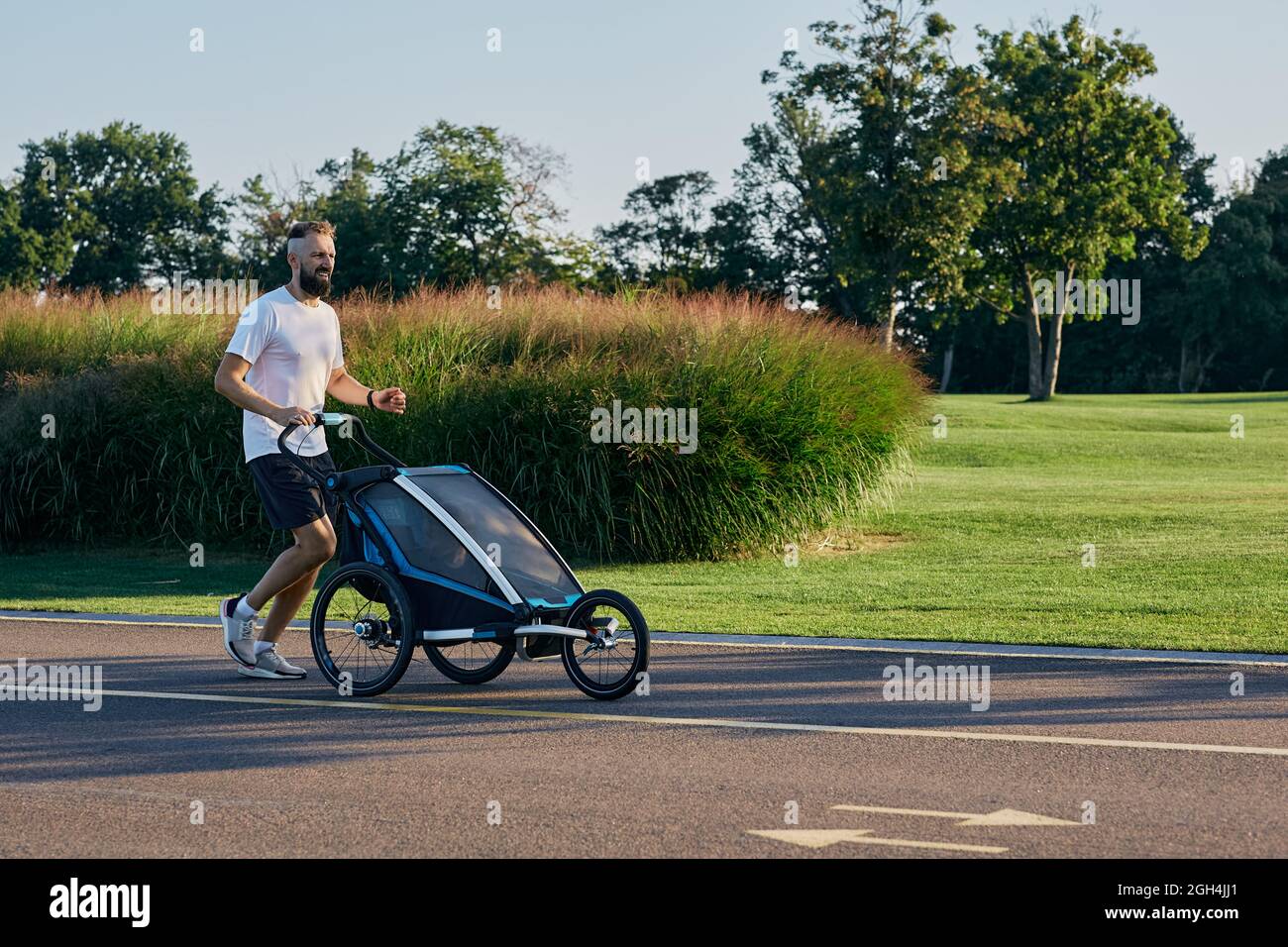 Young father with his kid in a jogging stroller during jogging in a ...