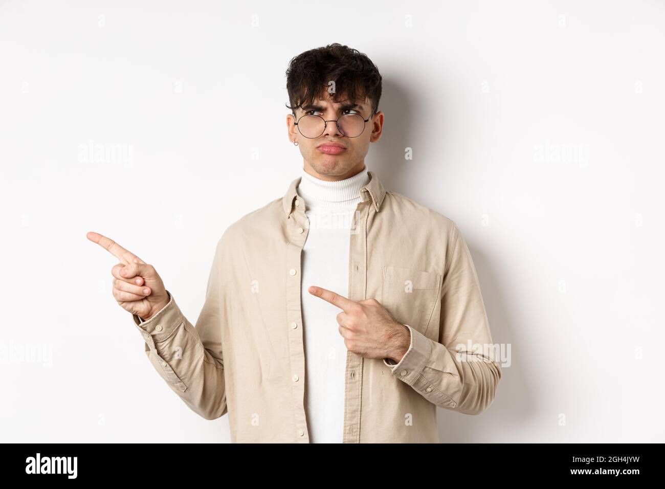 Disappointed guy in glasses looking and pointing left, sulking ...