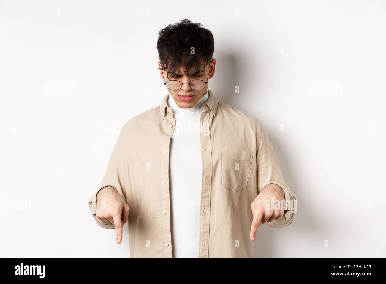 Confused frowning guy in glasses looking, pointing fingers down at ...