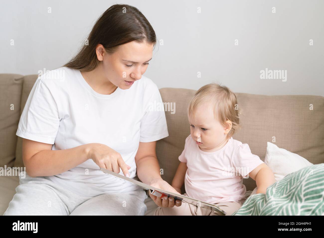 Mother explaining things while blond baby girl looking at book. Sitting ...
