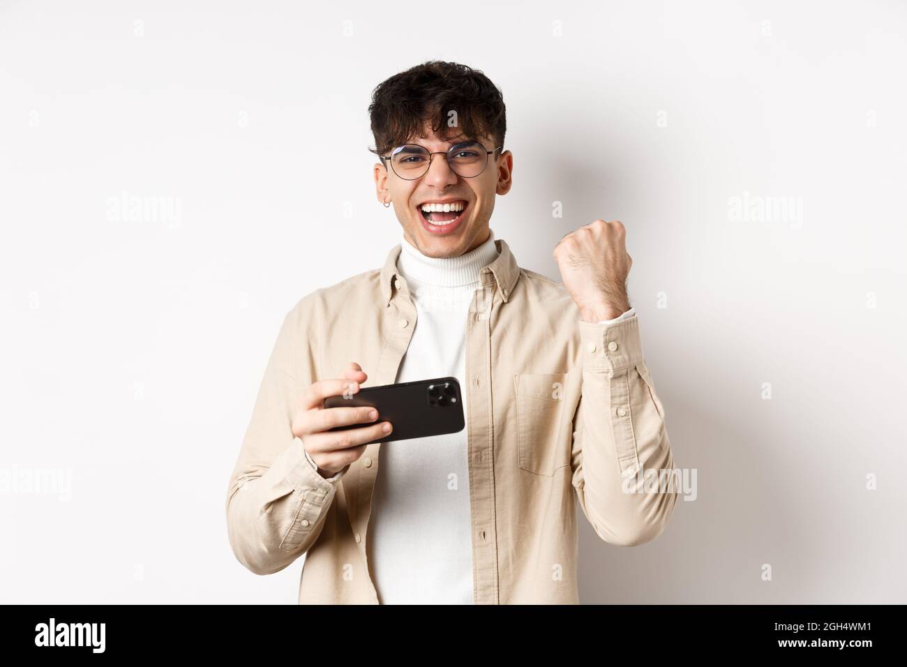 Happy guy winning on smartphone, holding mobile phone and raising hand ...