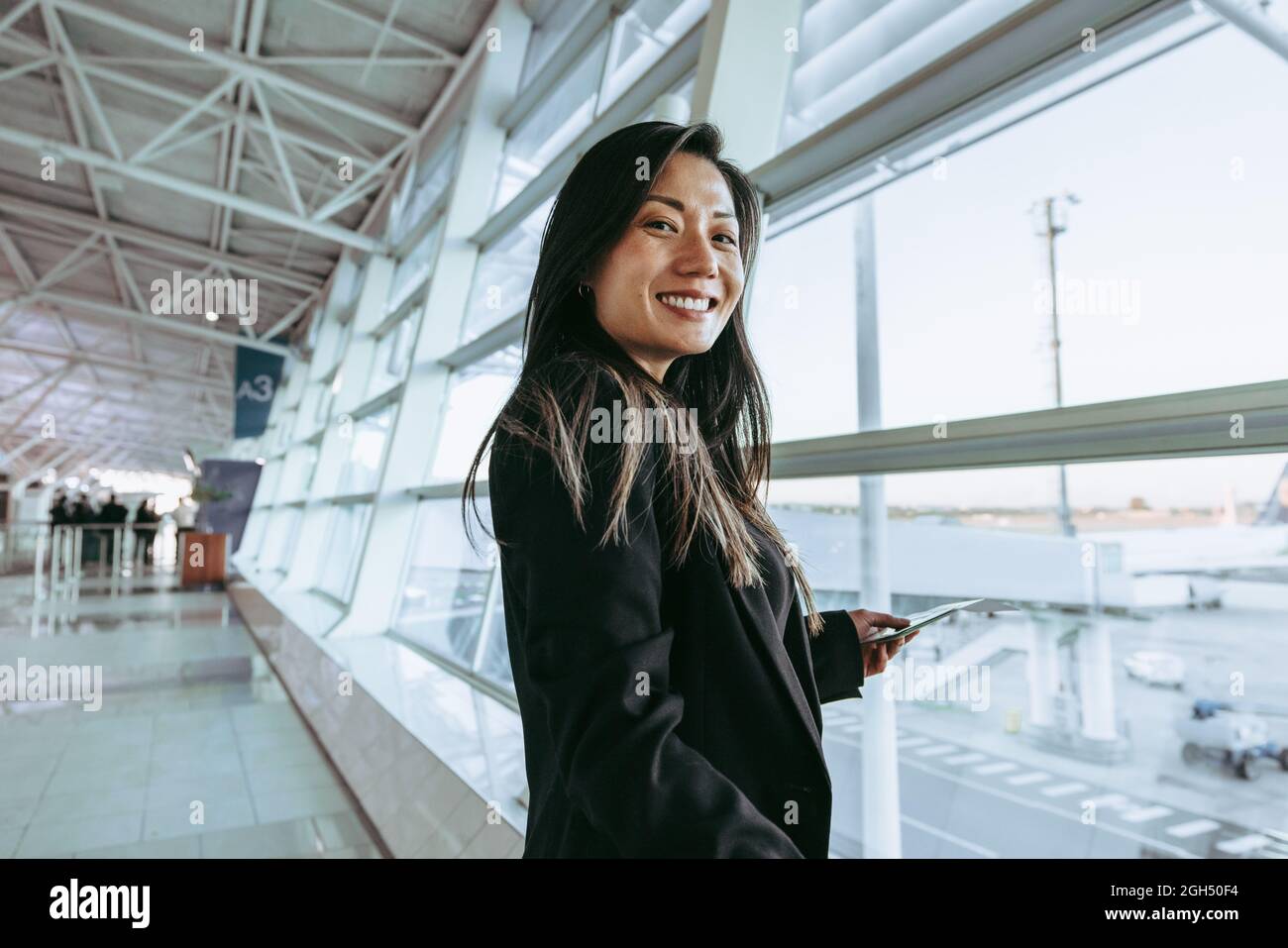 Smiling female passenger standing at airport terminal. Woman traveler waiting for flight at ...