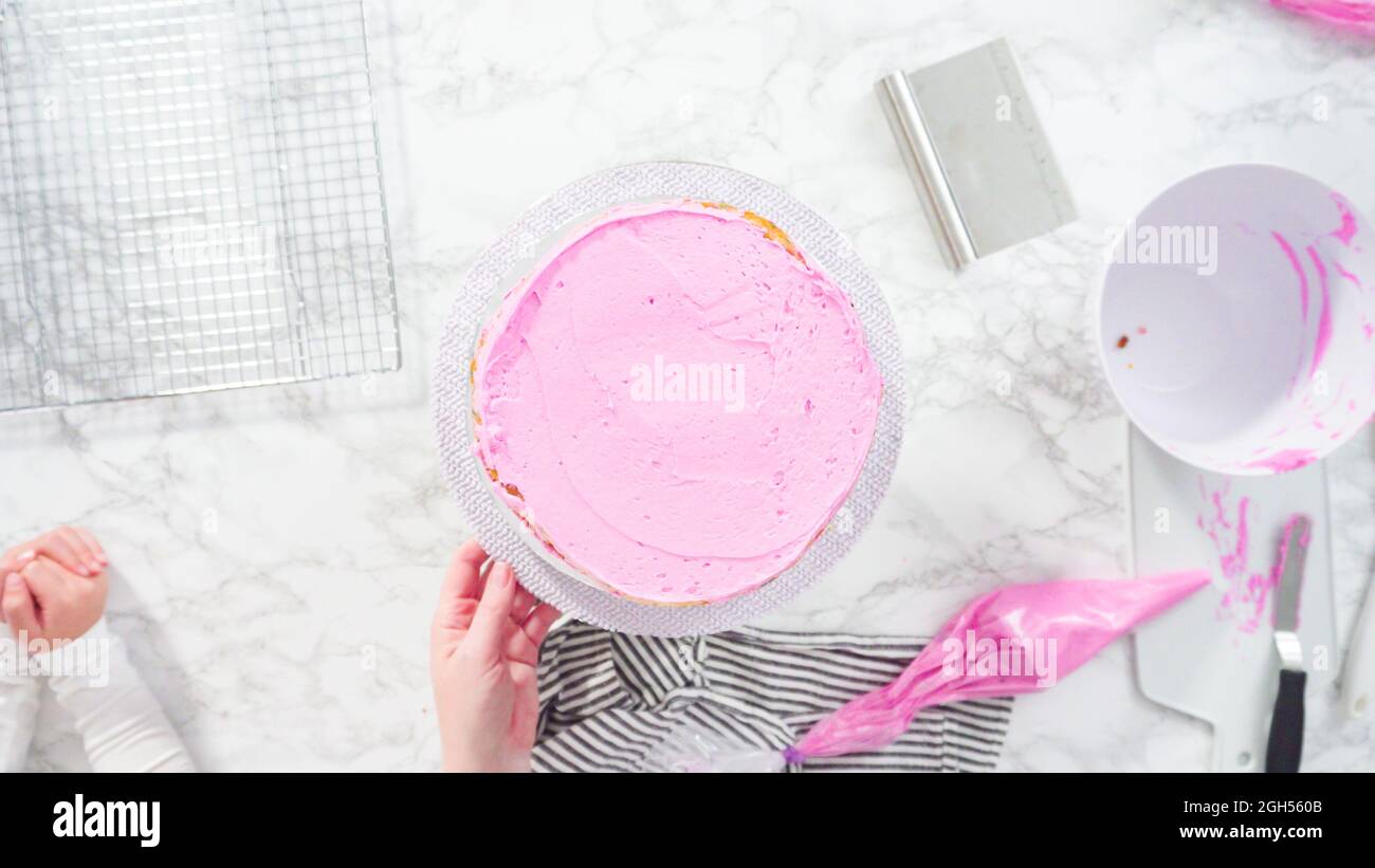 Flat lay. Step by step. Frosting round funfetti cake layers with pink ...