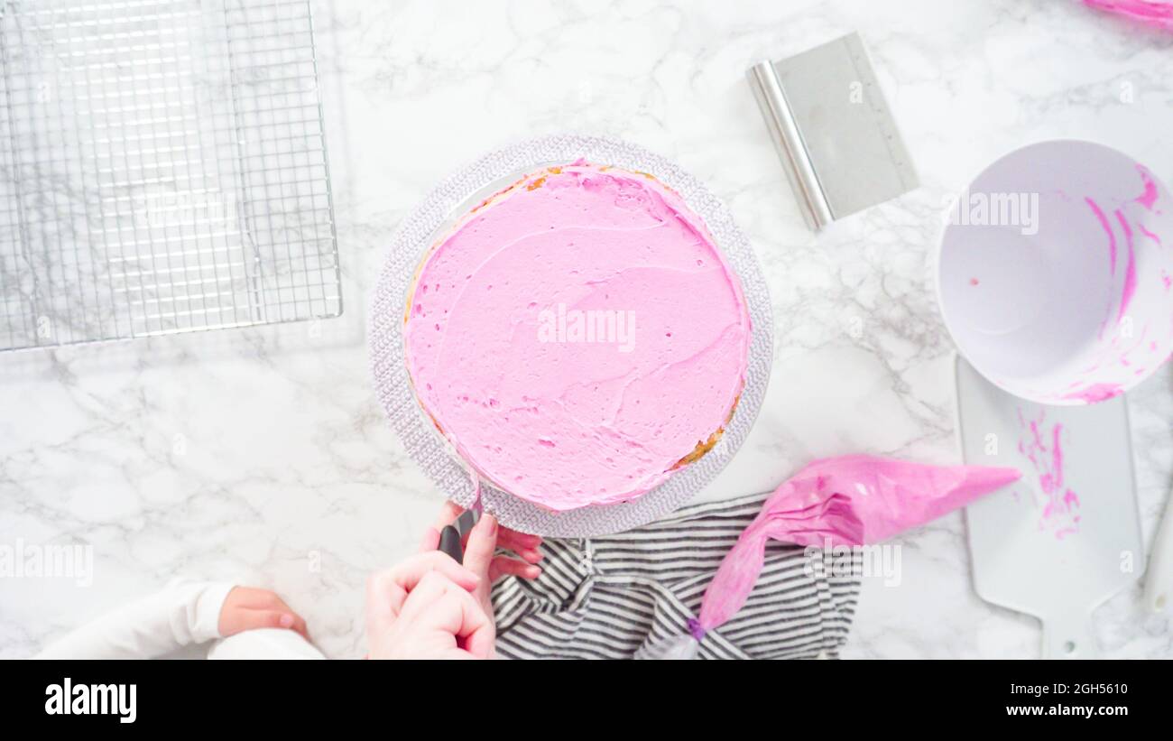 Flat lay. Step by step. Frosting round funfetti cake layers with pink ...
