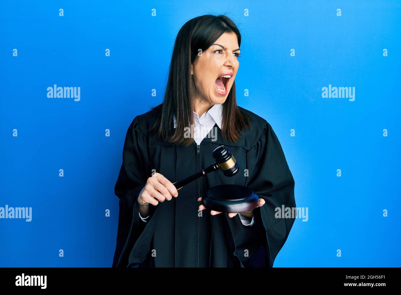 Young hispanic woman using gavel angry and mad screaming frustrated and ...