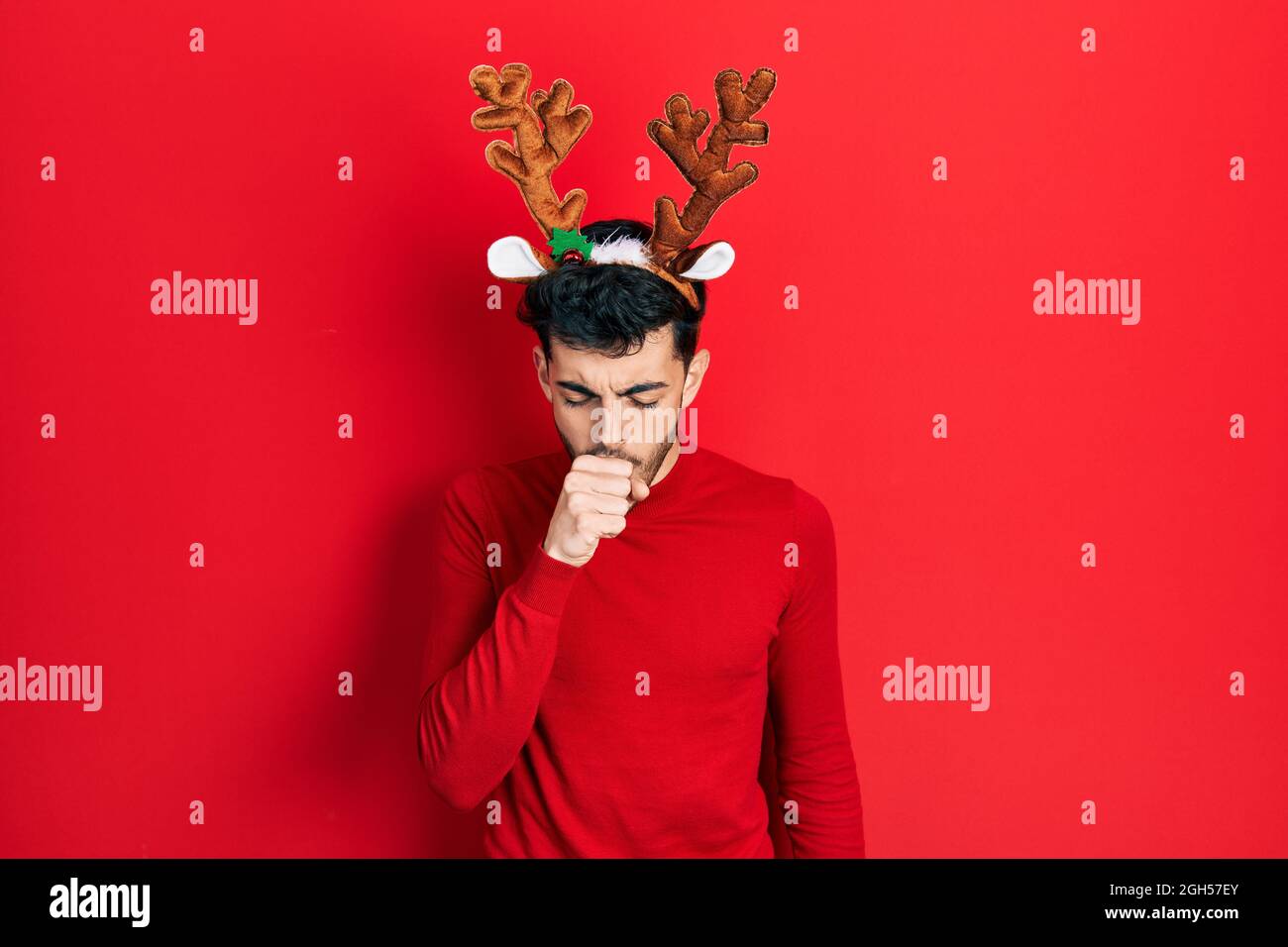Young hispanic man wearing cute christmas reindeer horns feeling unwell ...