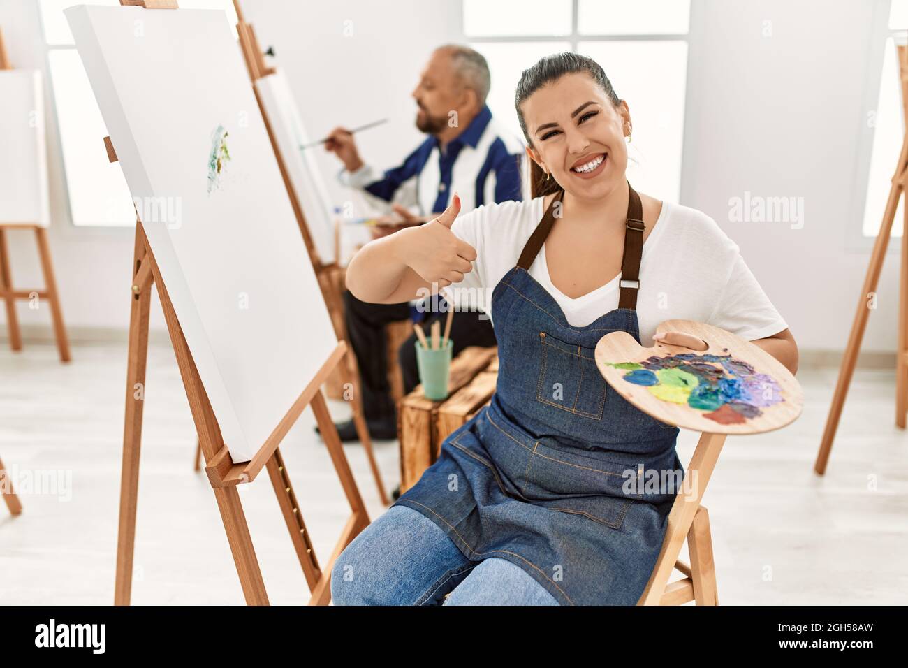 Young artist woman at art studio smiling happy and positive, thumb up ...
