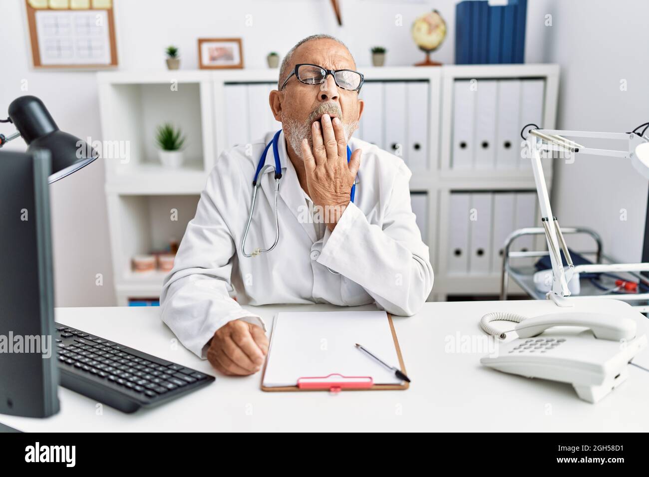 Mature doctor man at the clinic bored yawning tired covering mouth with ...