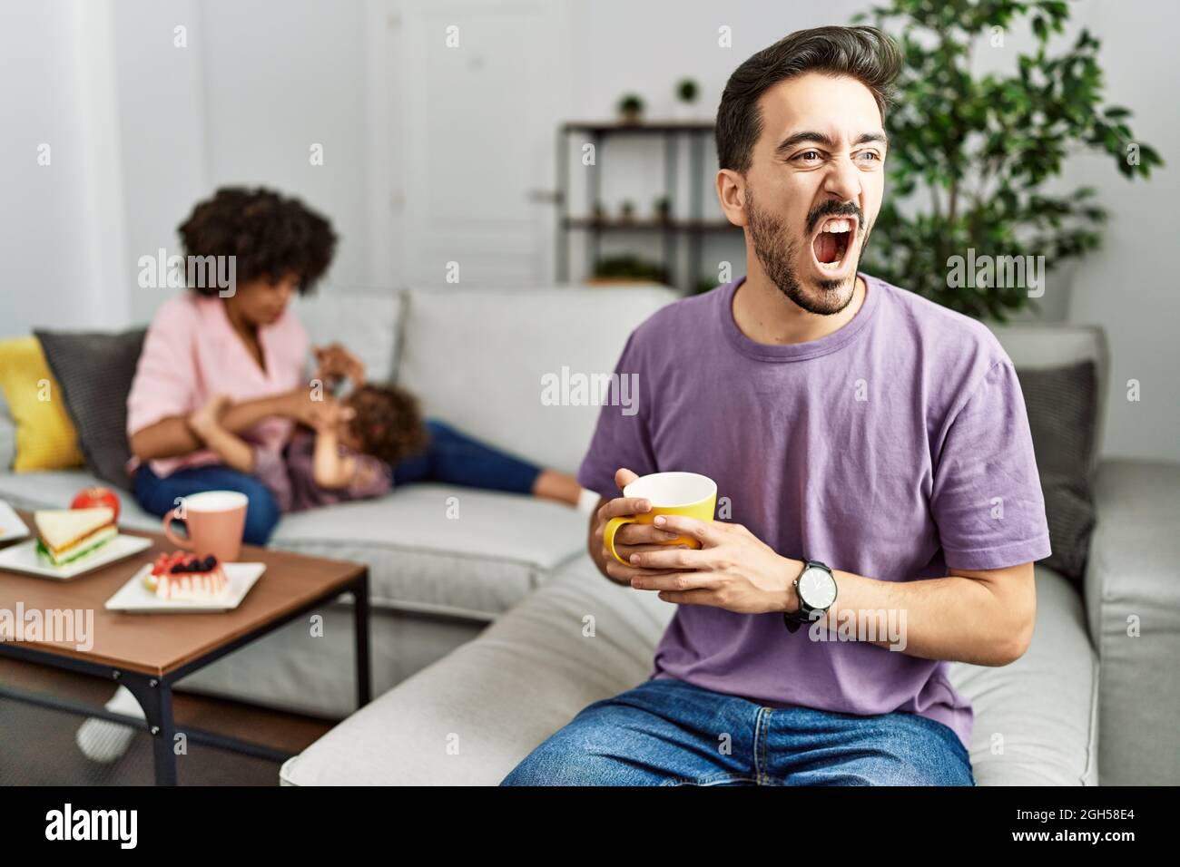 Hispanic father of interracial family drinking a cup coffee angry and ...