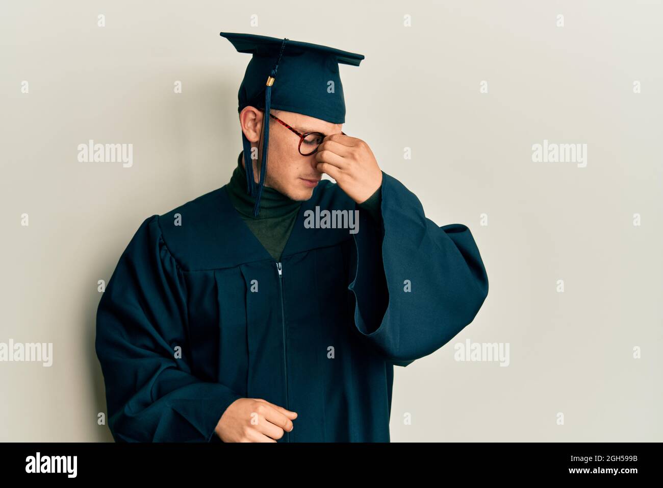 Young caucasian man wearing graduation cap and ceremony robe tired ...