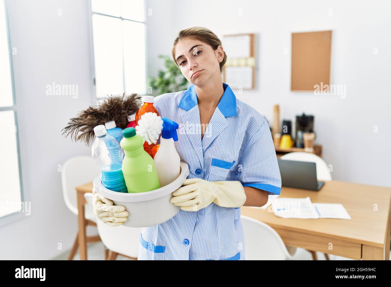 Young blonde woman wearing cleaner uniform holding cleaning products ...