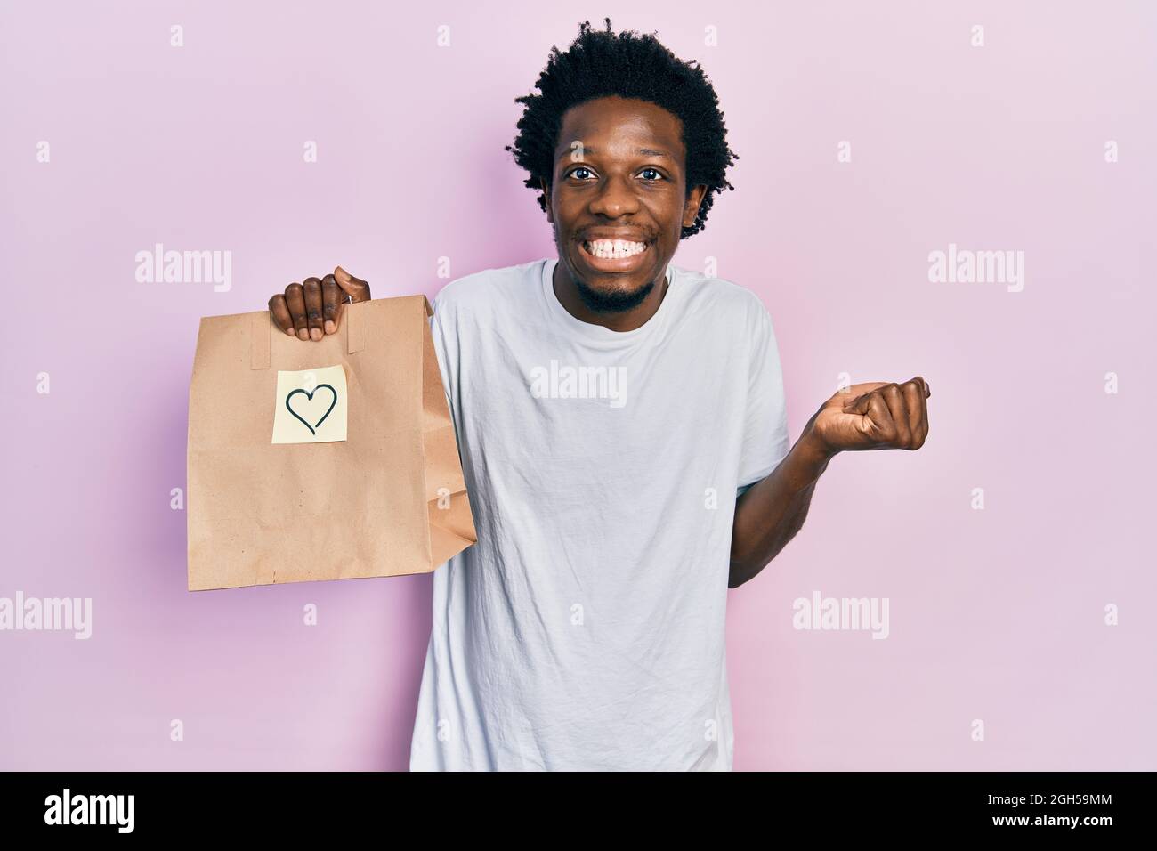 Young african american man holding take away paper bag with heart ...