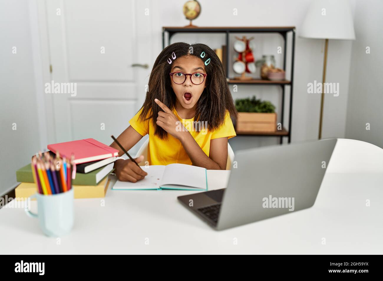 Young african american girl doing homework at home surprised pointing ...
