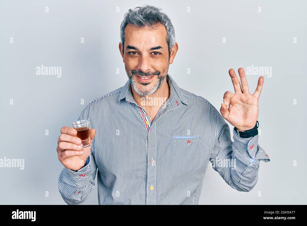 Handsome middle age man with grey hair drinking whiskey shot doing ok ...