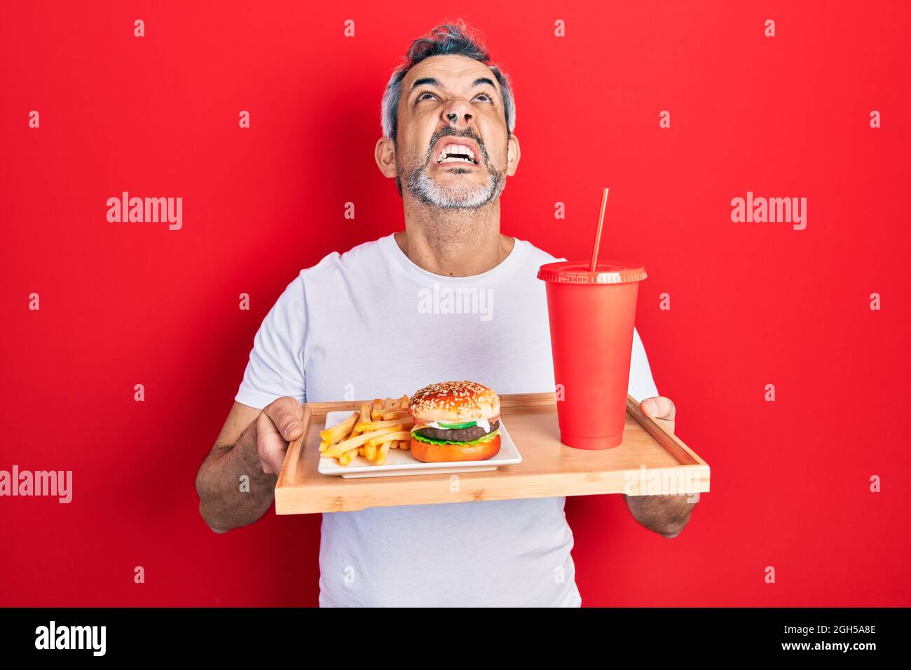 Handsome middle age man with grey hair eating a tasty classic burger ...
