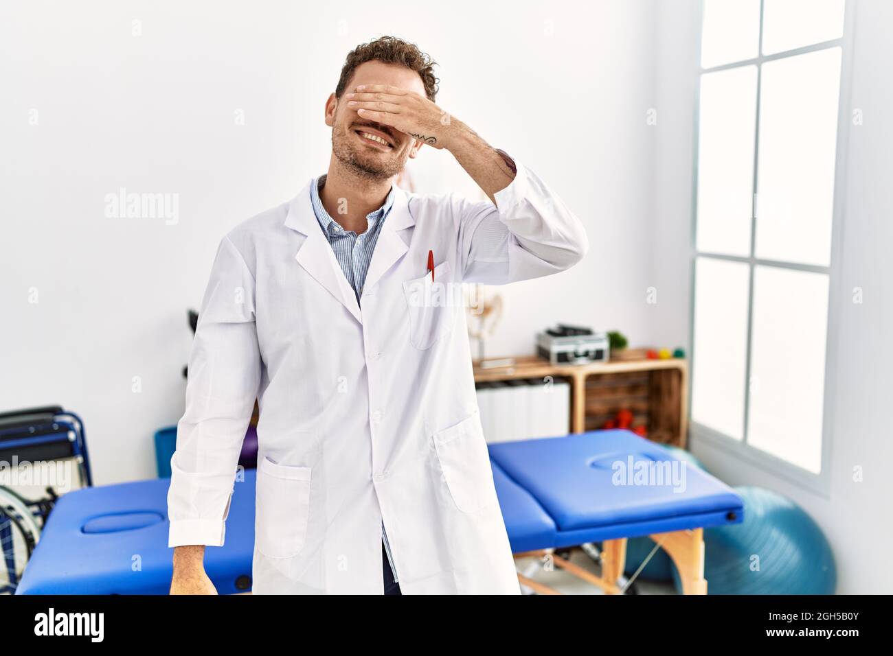Handsome young man working at pain recovery clinic smiling and laughing ...