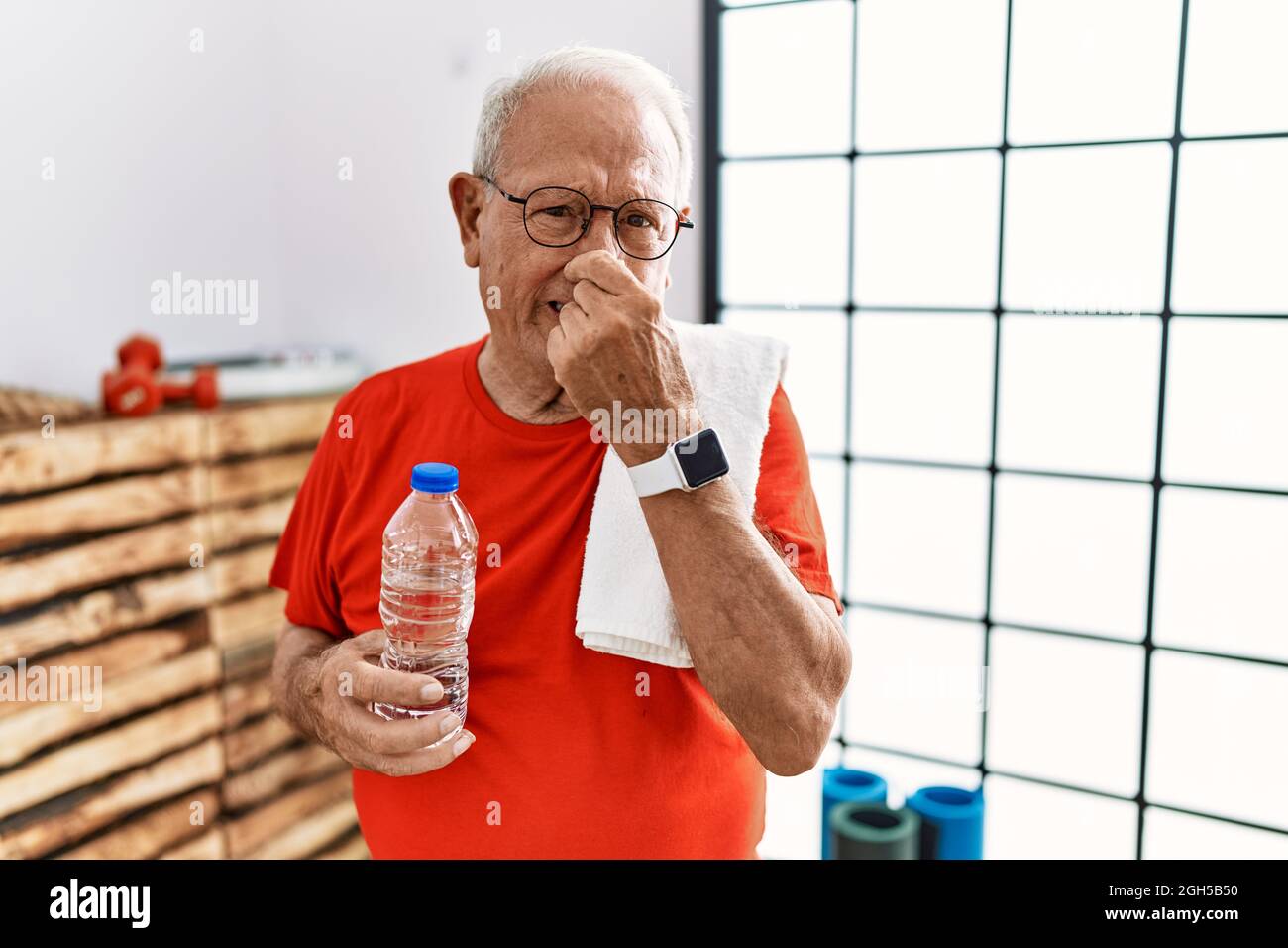 Senior man wearing sportswear and towel at the gym smelling something ...