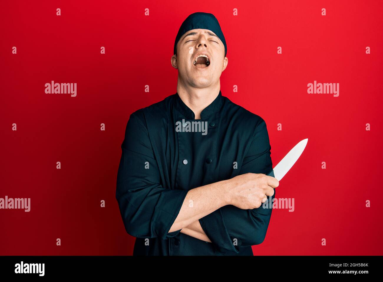 Handsome young man wearing professional cook uniform holding knife ...