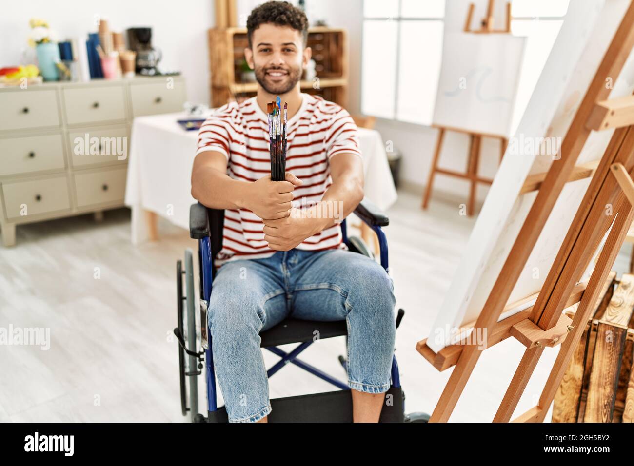 Young arab disabled artist man holding paintbrushes sitting on ...