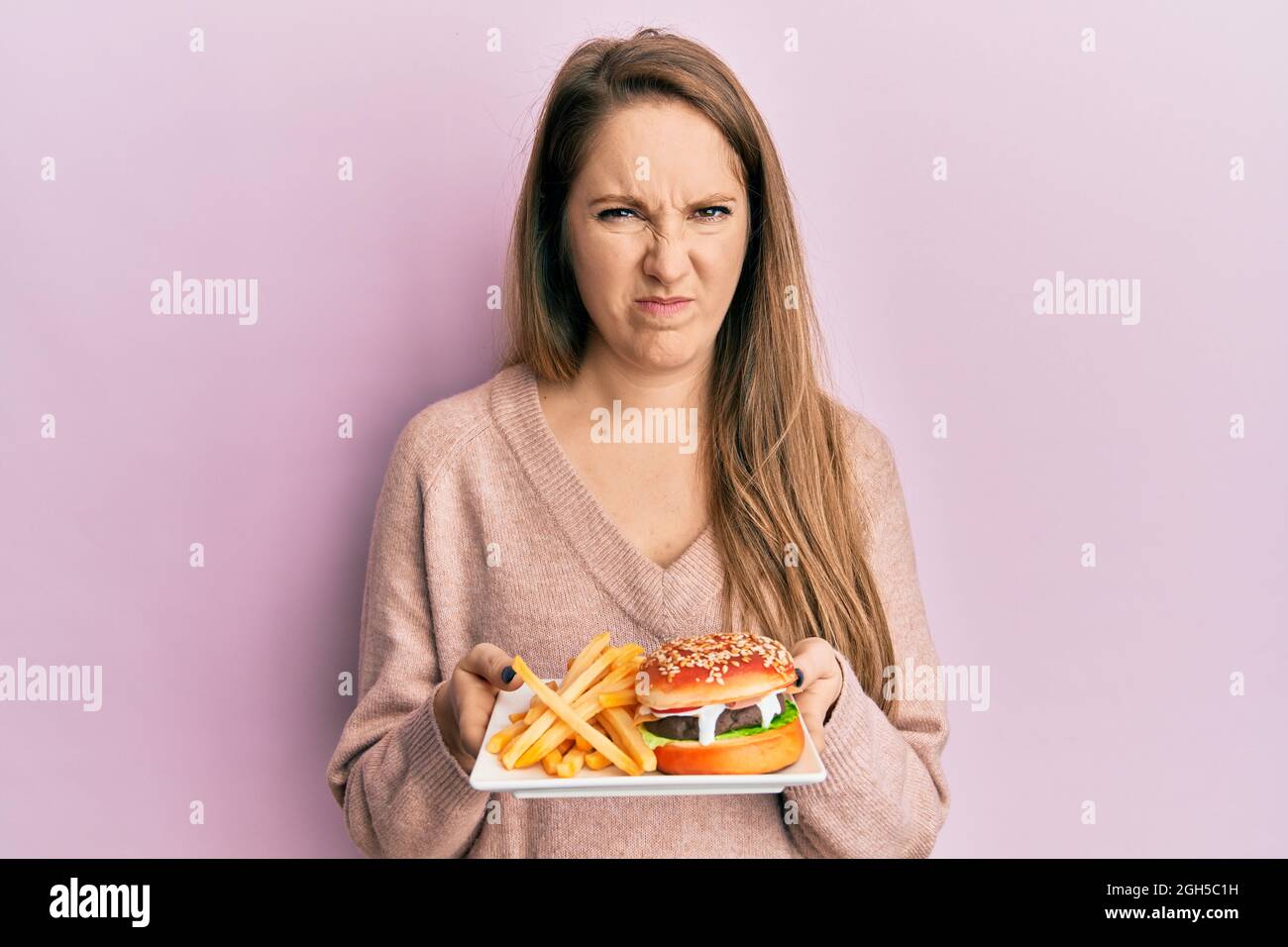 Young blonde woman eating a tasty classic burger with fries skeptic and ...