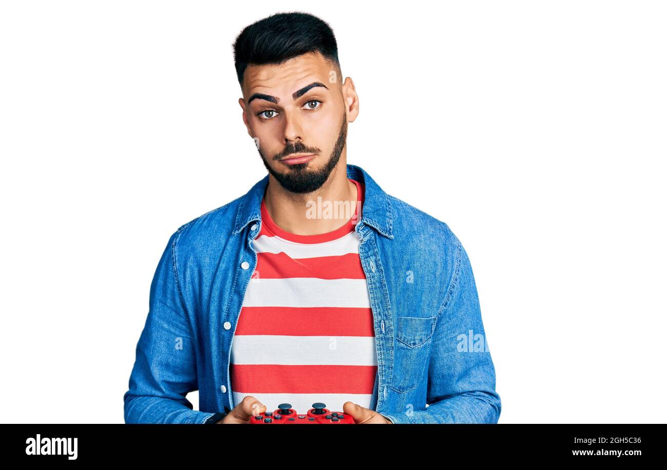 Young hispanic man with beard playing video game holding controller ...