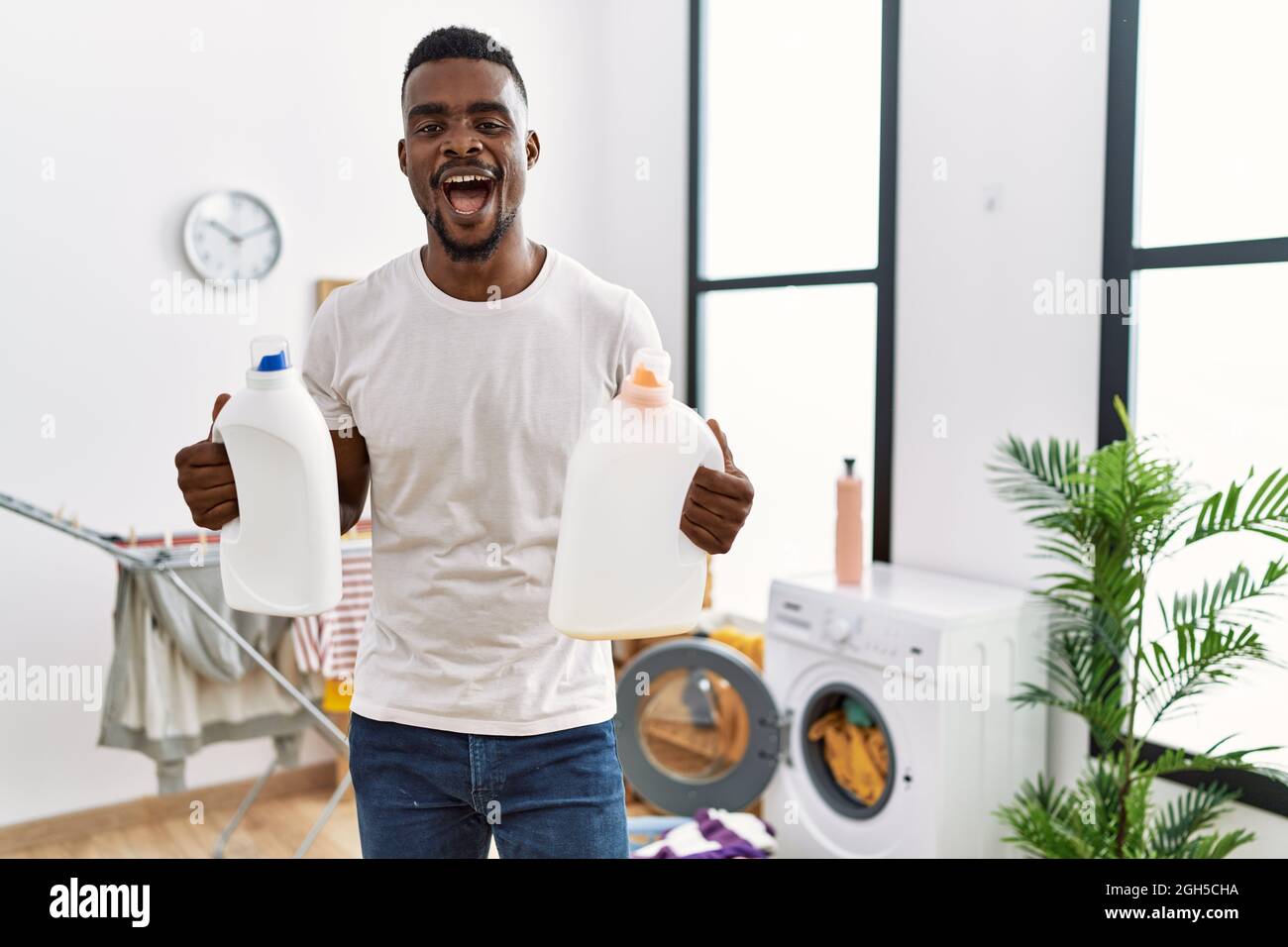 Young african man doing laundry holding detergent bottles smiling and ...